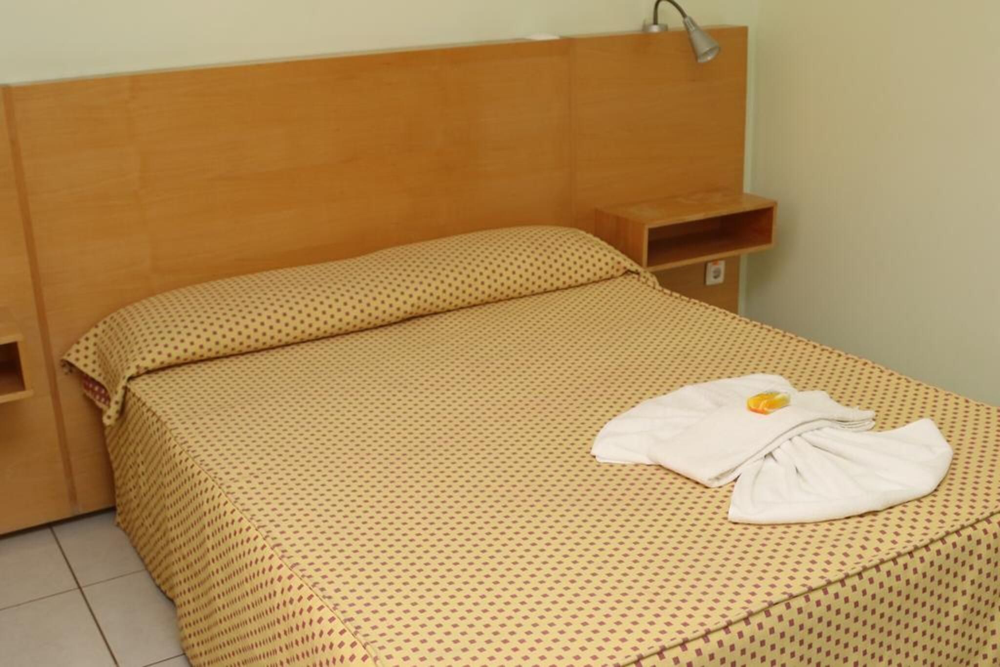 Uma cama de solteiro com cabeceira, mesa de cabeceira e luminária na parede.