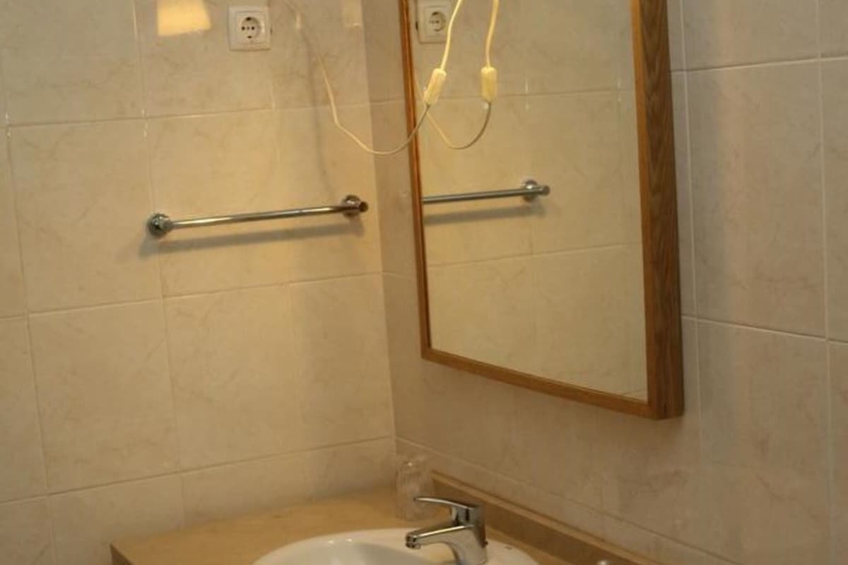 Um banheiro com pia, espelho, porta-toalhas e luminária na parede.