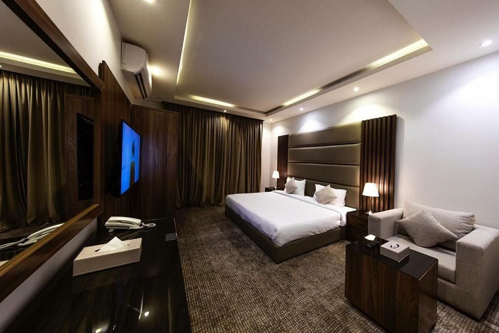 Quarto de hotel moderno com uma cama grande, um sofá, uma TV e uma mesa com telefone e uma caixa.