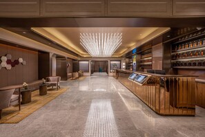 Um lobby moderno com área de bar, assentos e uma luminária decorativa no teto.