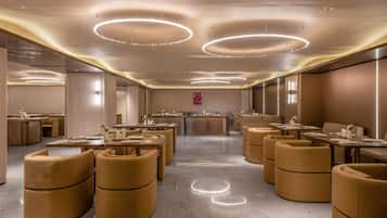 Um lobby de hotel moderno com mesas redondas, assentos acolchoados e um balcão de recepção central.