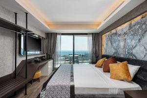 Quarto de hotel moderno com uma cama grande, uma escrivaninha, televisão de tela plana e varanda com vista para o mar.