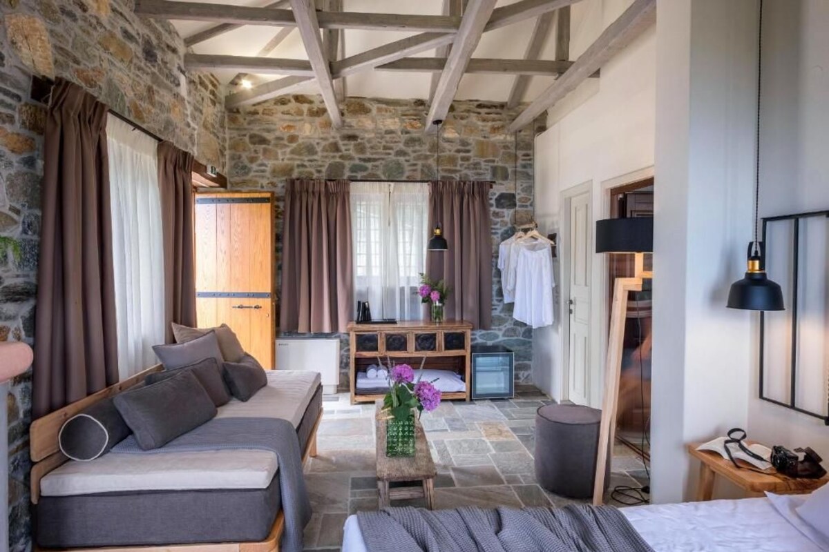 Quarto aconchegante com parede de pedra, um banco de madeira, uma cama e uma pequena mesa com um vaso.