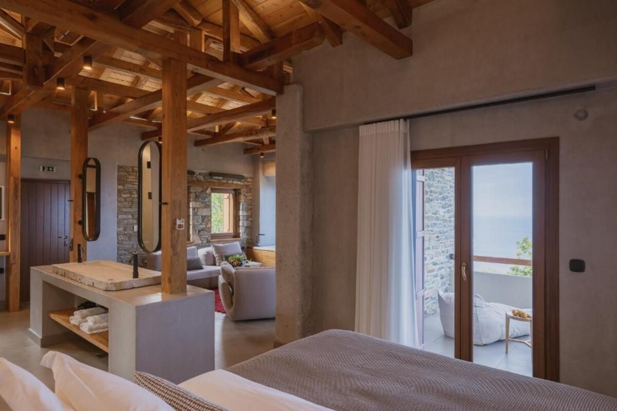 Quarto moderno com cama grande, teto de madeira, paredes de pedra e varanda com vista.