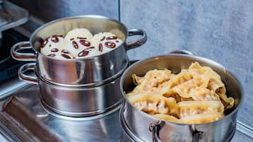 Duas panelas de aço inoxidável em um fogão, uma com dumplings e outra com uma substância branca e sementes vermelhas.