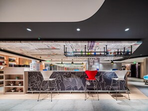 Uma área de bar moderna com um design de teto único, um balcão com banquetas e uma parede com desenhos artísticos.