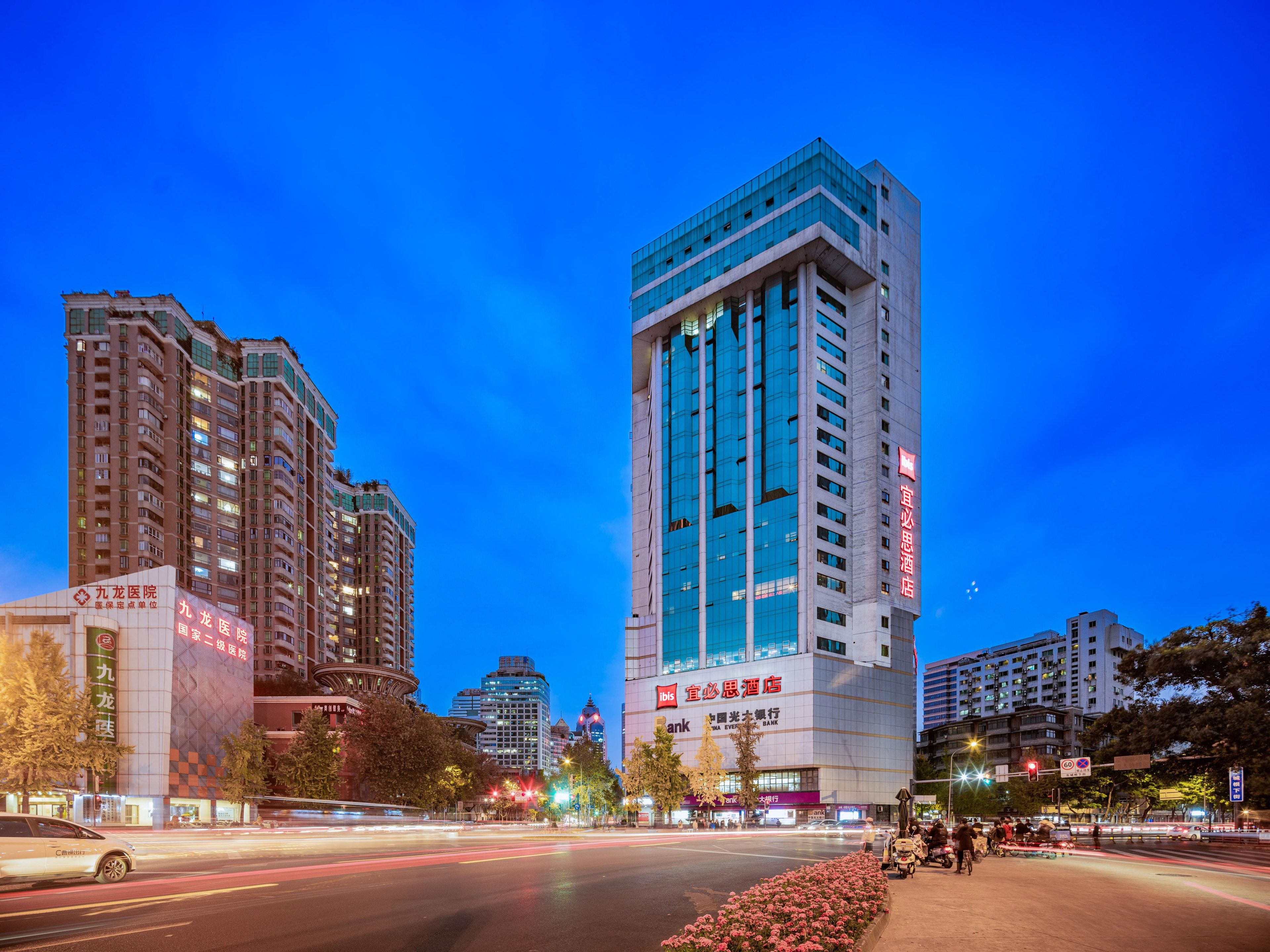Um edifício alto com vários andares, um sinal de banco bem visível e uma grande placa iluminada na lateral.