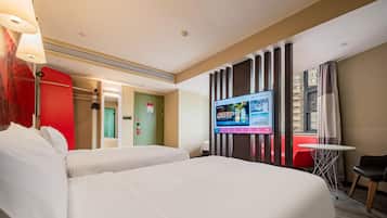 Quarto de hotel com duas camas, televisão na parede, uma mesinha e janela com cortinas.