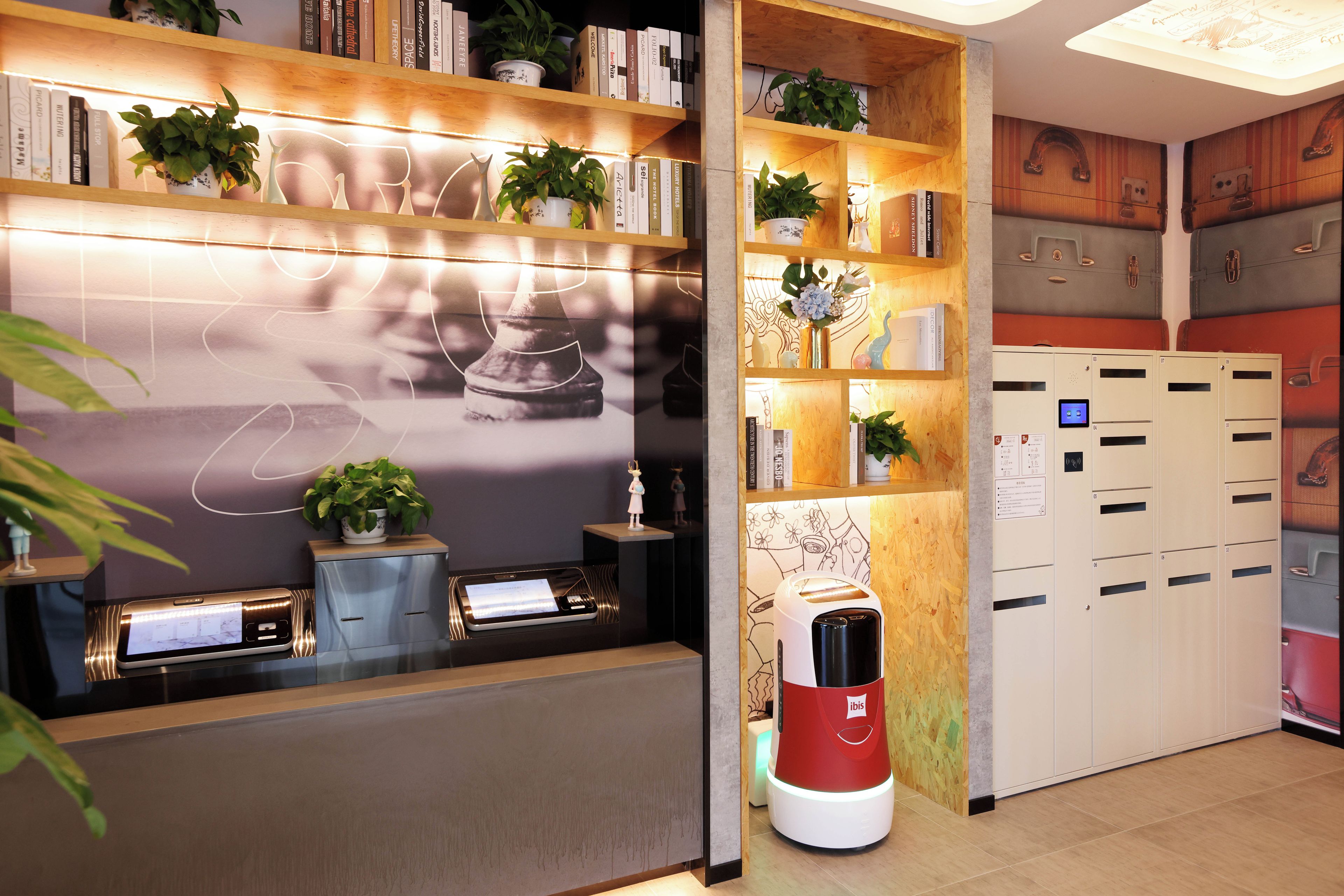 Uma área de recepção com um quiosque digital, estantes com plantas e uma máquina de café.