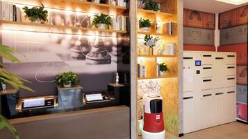 Uma área de recepção com um quiosque digital, estantes com plantas e uma máquina de café.