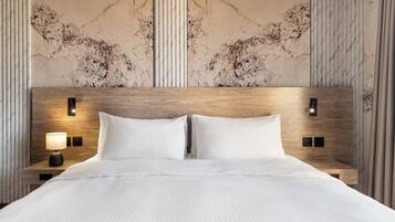 Quarto de hotel com uma cama grande, cabeceira de madeira, duas luminárias de cabeceira e parede com padrão marmorizado.