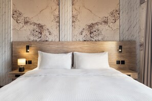 Quarto de hotel com uma cama grande, cabeceira de madeira, duas luminárias de cabeceira e parede com padrão marmorizado.