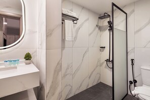 Casa de banho moderna com chuveiro, sanita e lavatório com artigos de higiene pessoal.