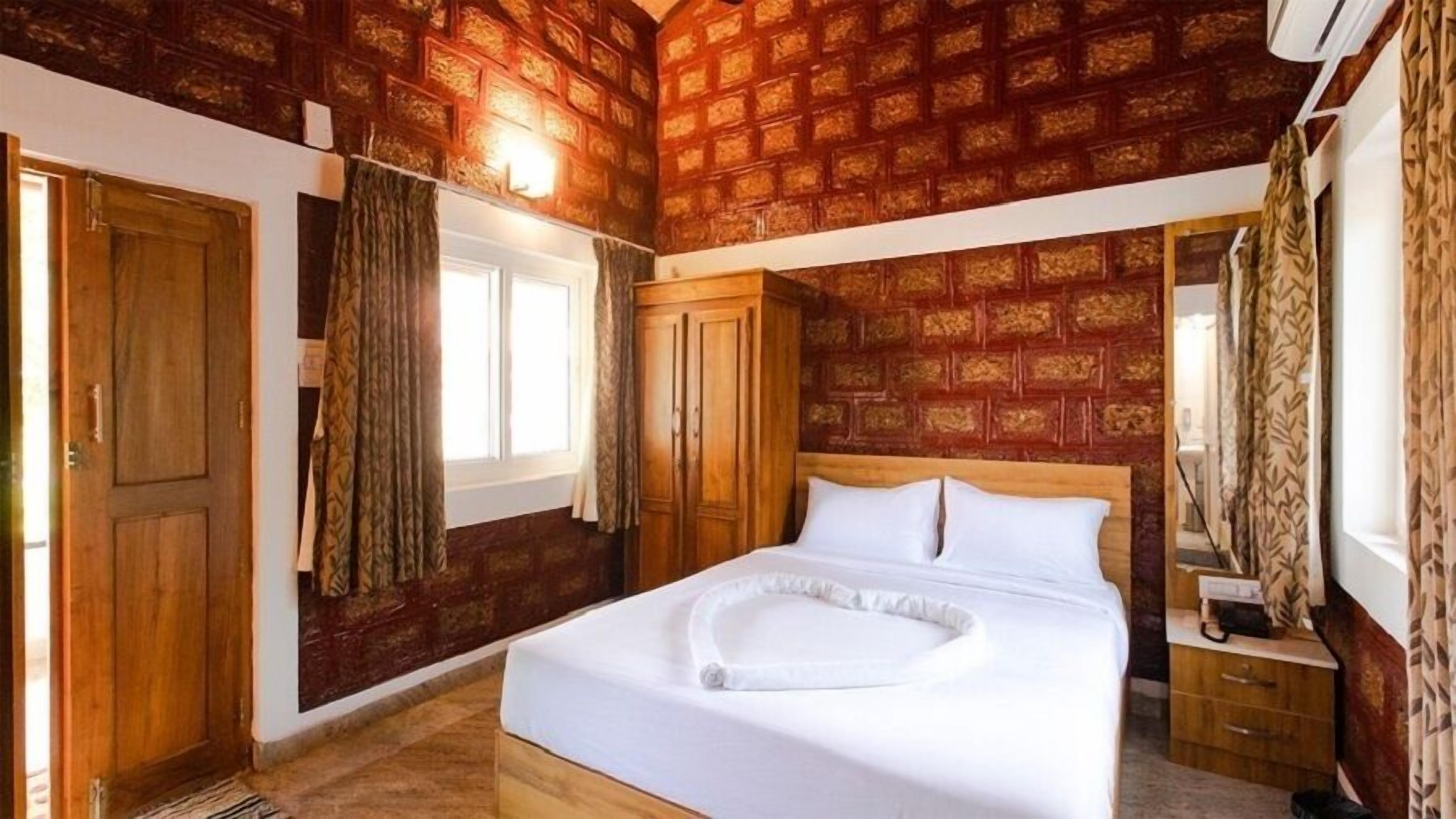 Quarto com cabeceira de madeira, cama com roupa de cama branca, guarda-roupa de madeira e janela com cortinas.