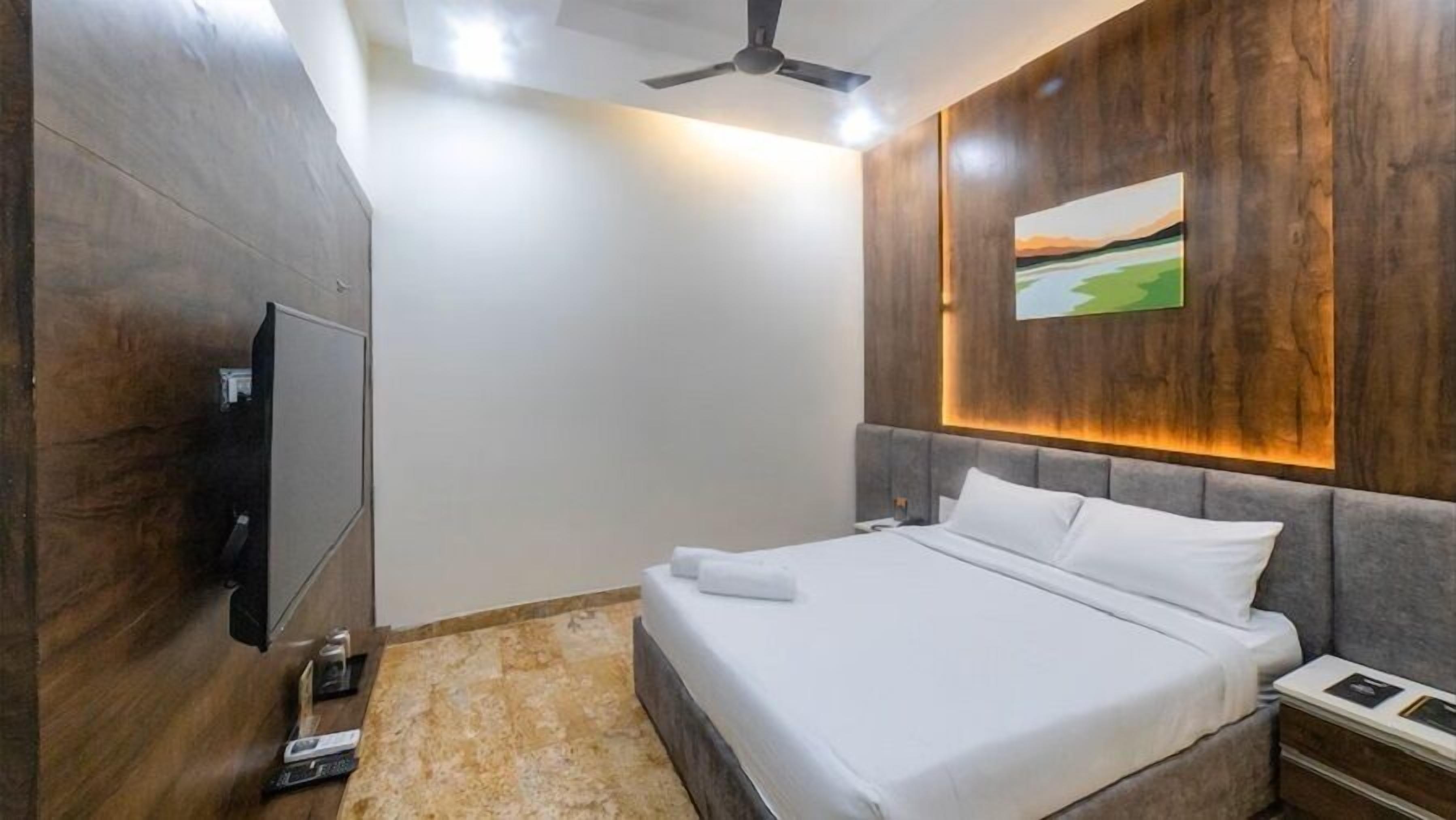 Quarto de hotel com cama, televisão, ventoinha no teto e um quadro na parede.