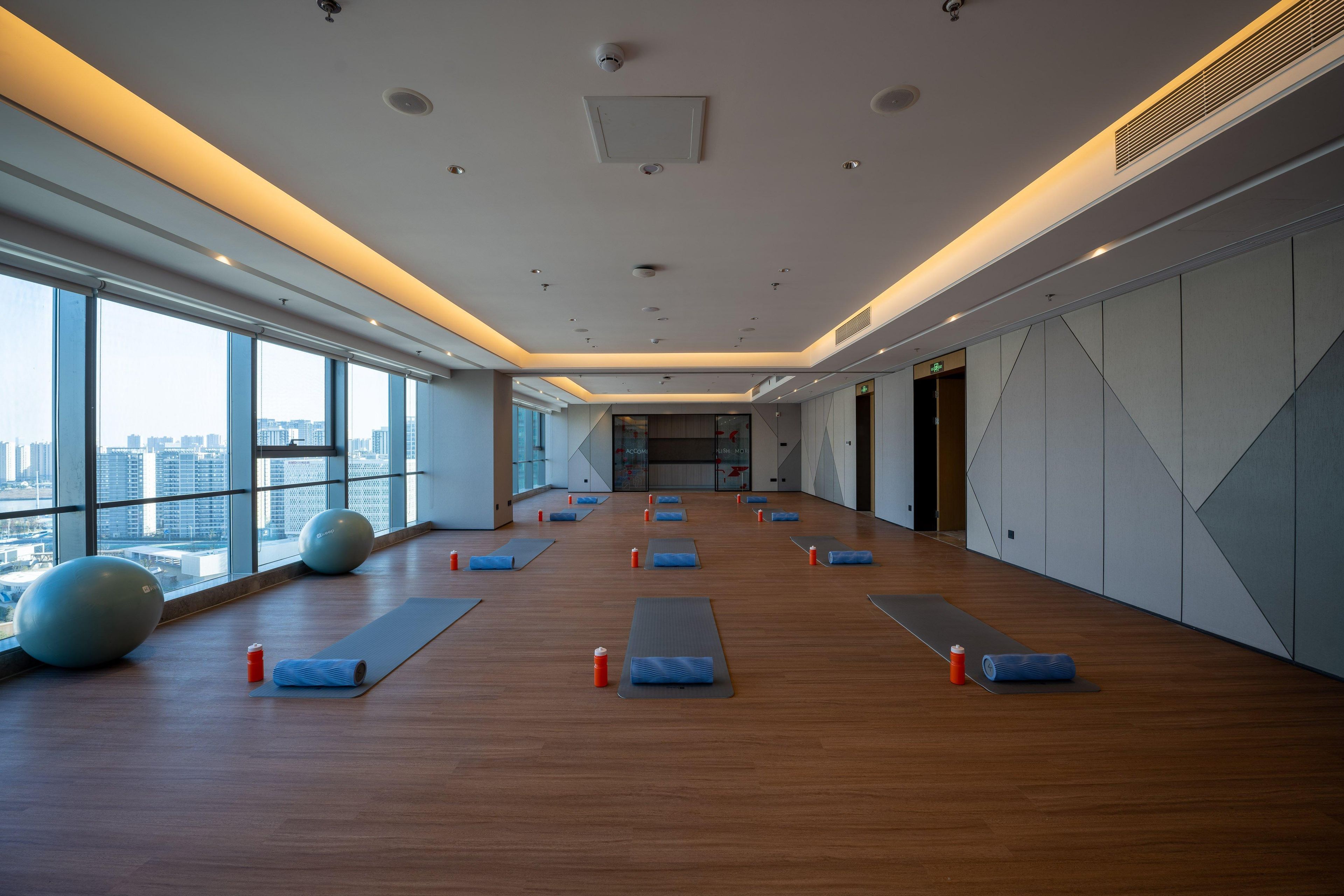 Quarto amplo com grandes janelas, equipamentos de ginástica e vista para a cidade.