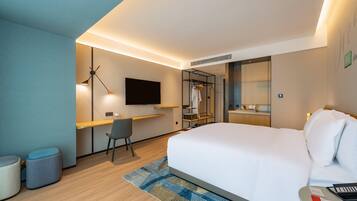Quarto de hotel moderno com cama, escrivaninha, cadeira e televisão de tela plana.
