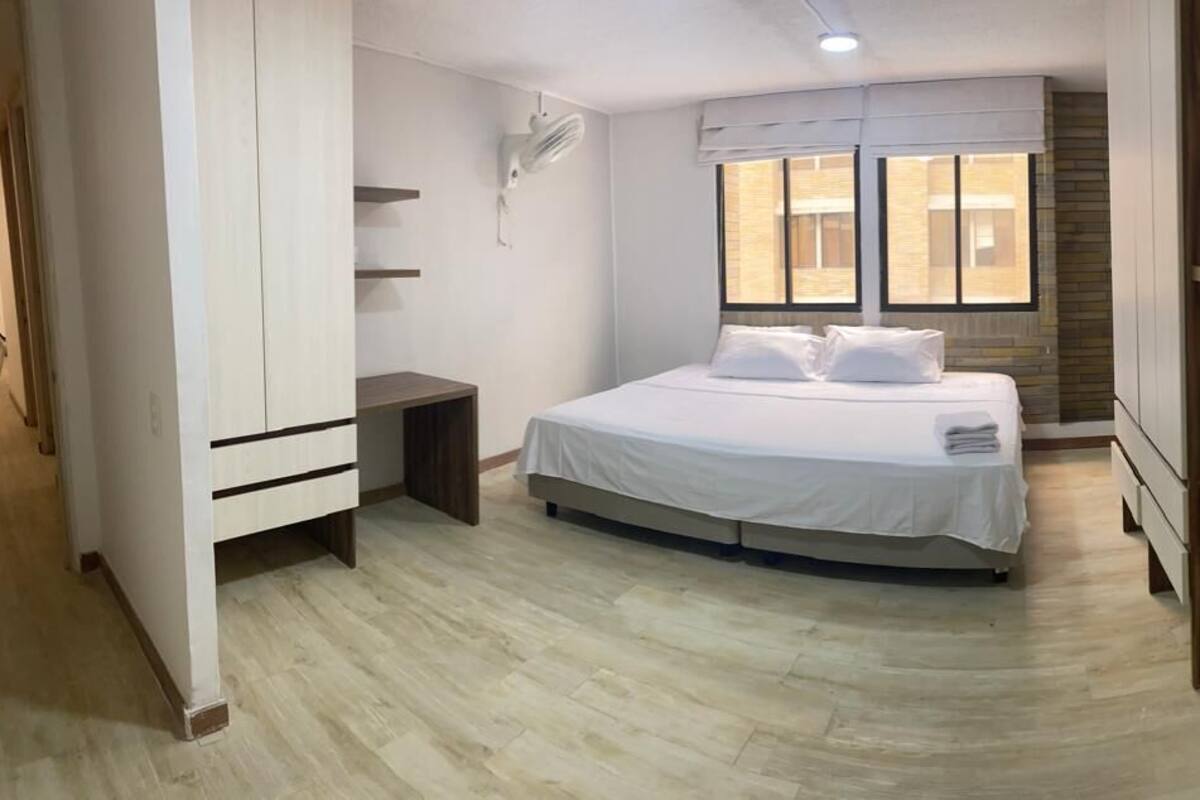 Quarto com cama, mesas de cabeceira, guarda-roupa e janela com persianas.