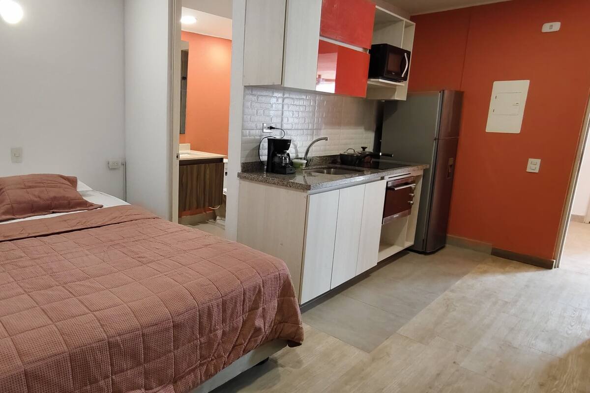 Quarto com cama e cozinha compacta.