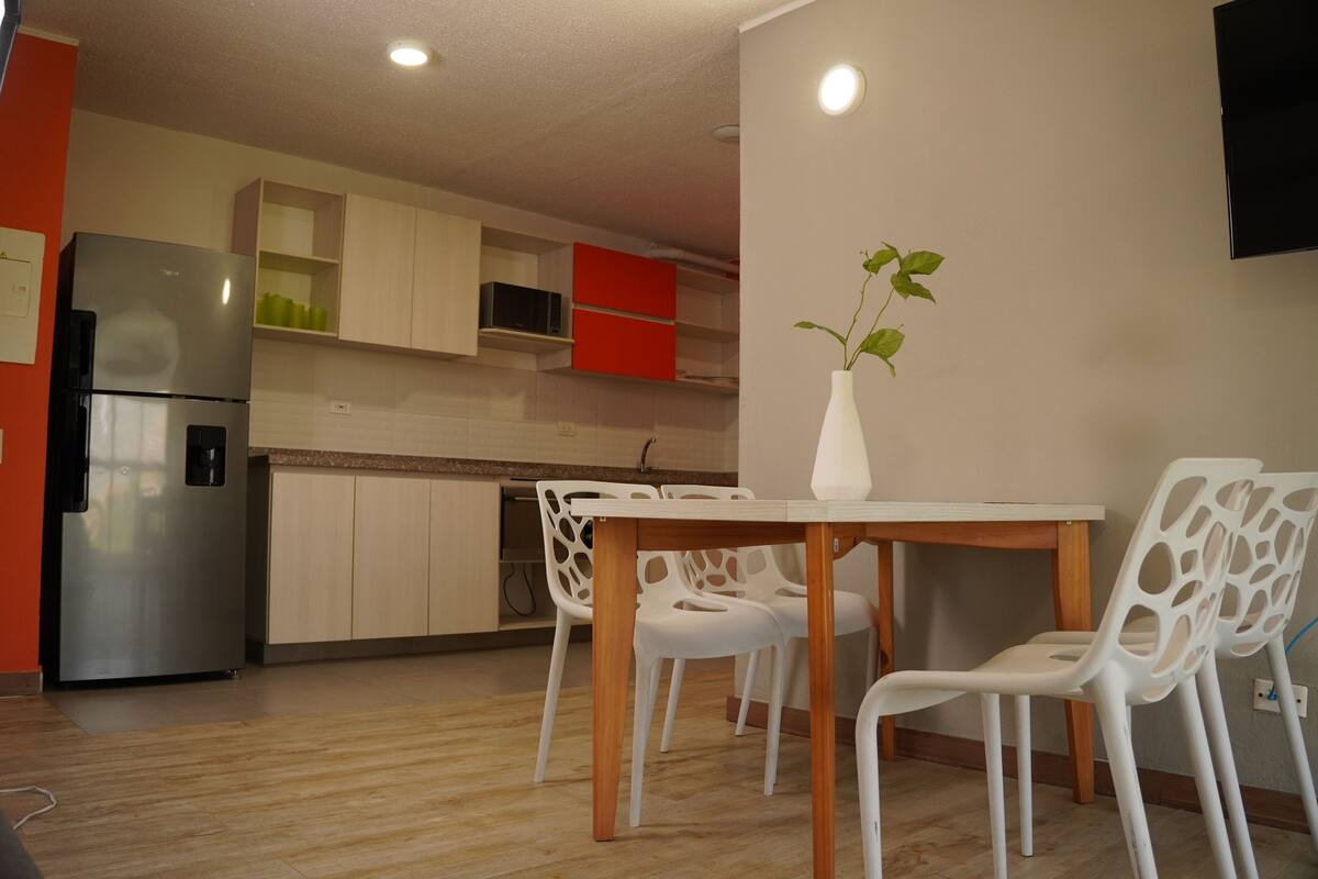 Uma cozinha moderna com armários brancos, uma geladeira de aço inoxidável e uma área de jantar com mesa e cadeiras brancas.