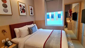 Quarto de hotel com cama, escrivaninha com telefone, obra de arte na parede, televisão e janela com vista.