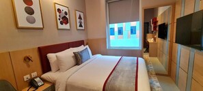 Quarto de hotel com cama, escrivaninha com telefone, obra de arte na parede, televisão e janela com vista.