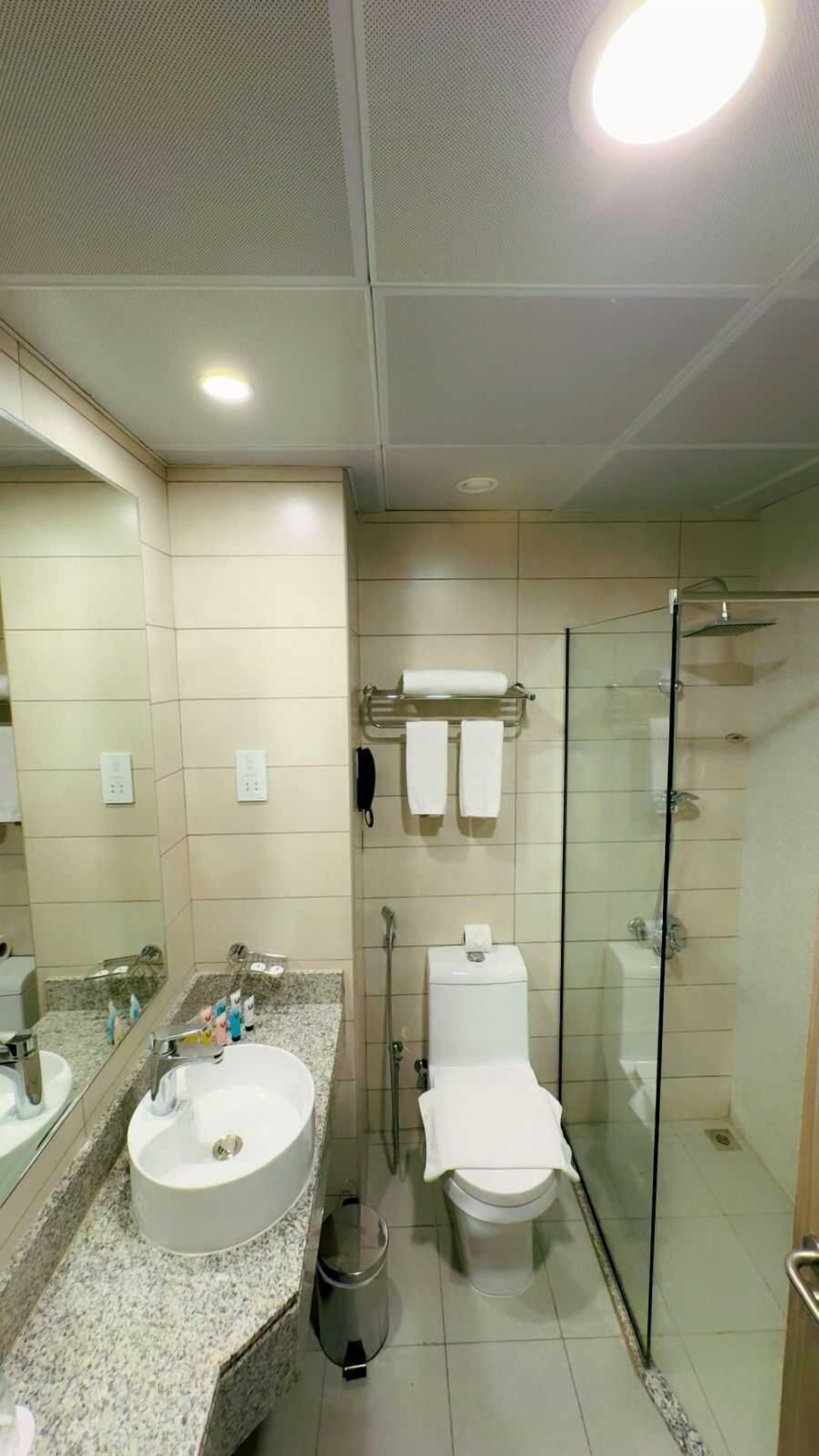 Casa de banho moderna com lavatório em bancada de granito, cabine de duche em vidro e sanita com suporte para toalhas de papel.