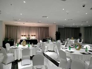 Uma sala de conferências com mesas redondas, cadeiras brancas e um palco com um púlpito.