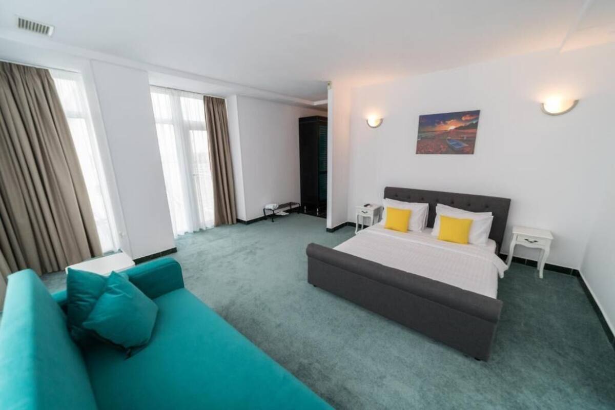 Quarto de hotel com cama, sofá verde, mesa pequena e um quadro na parede.