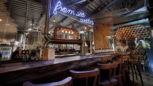 Um bar com um letreiro de néon que diz 'água do mar', banquetas de madeira e uma parede de garrafas de vinho.