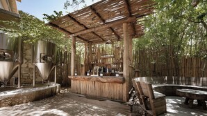 Uma área de bar ao ar livre com pergolado de madeira, colunas de pedra e um espaço para sentar.