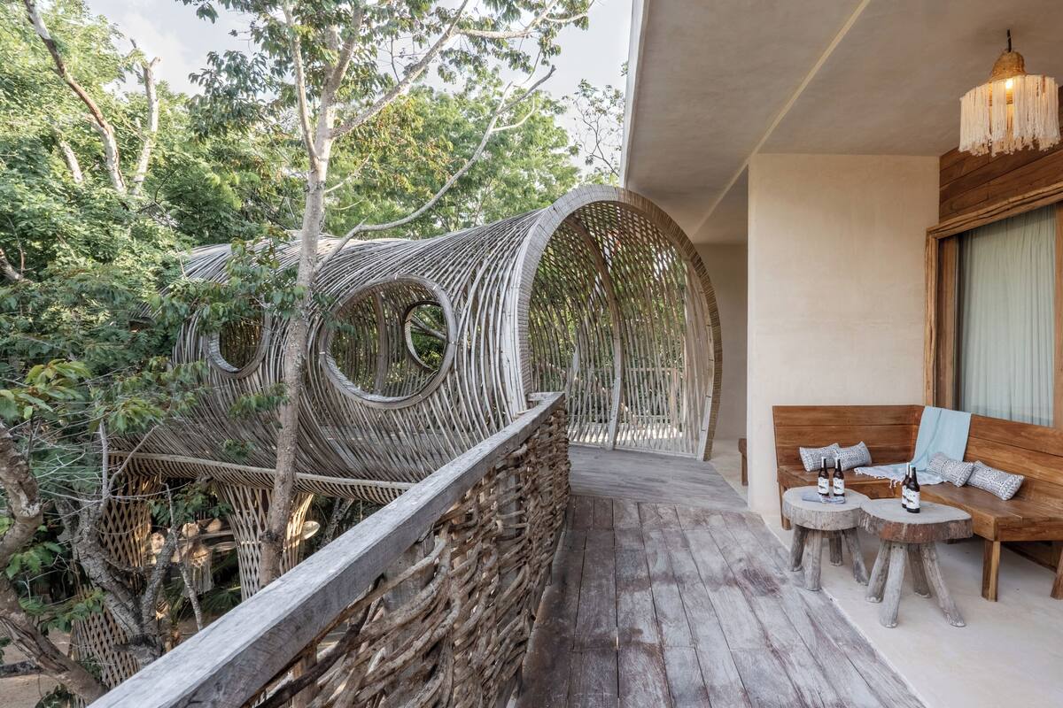Um deck de madeira com um toldo tecido, um banco de madeira e uma mesa com garrafas.