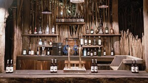 Um espaço de bar rústico com vigas de madeira, luminárias penduradas e prateleiras cheias de garrafas.