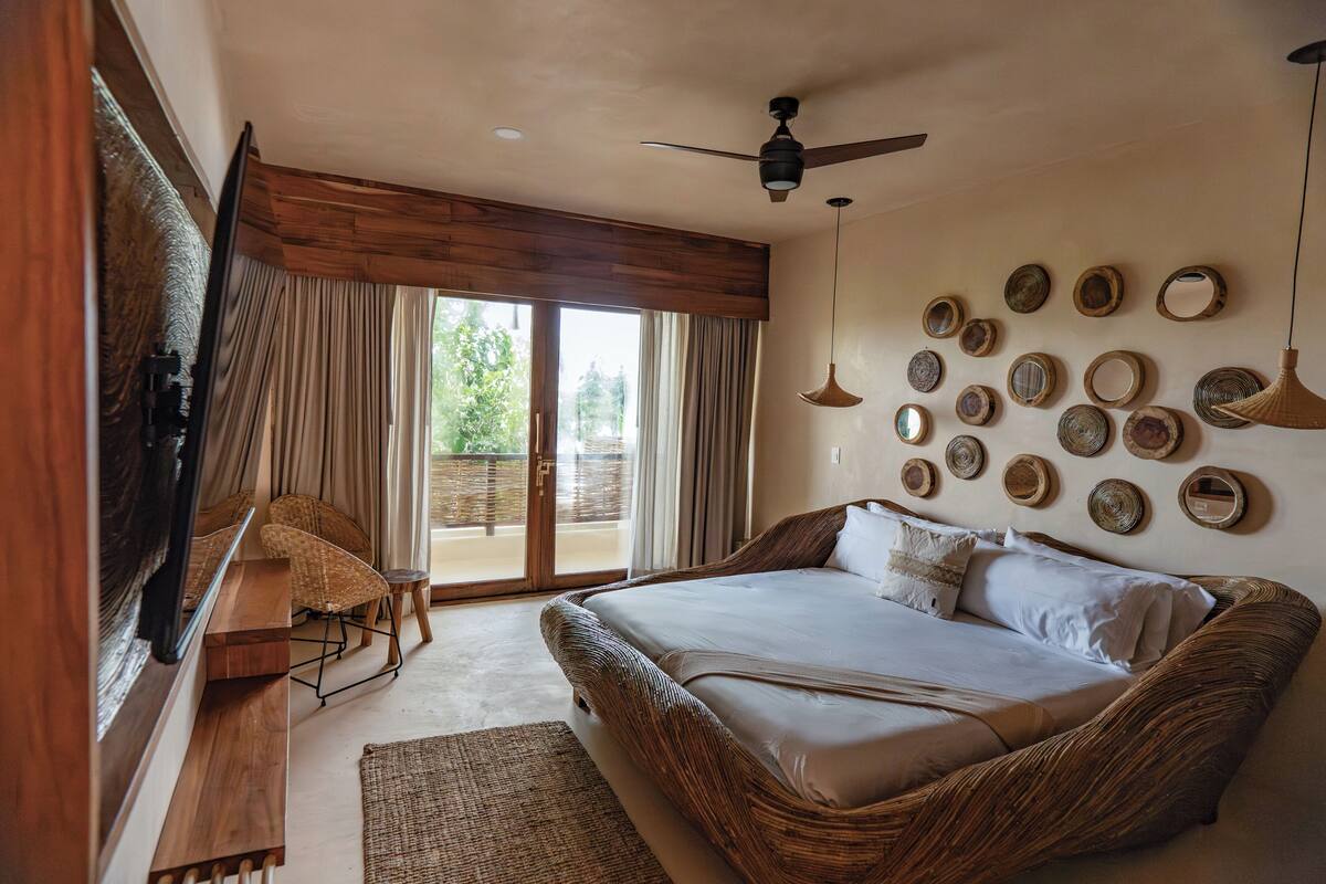 Quarto espaçoso com uma cama grande, ventoinha de teto de madeira e vista para o exterior através de portas de correr de vidro.