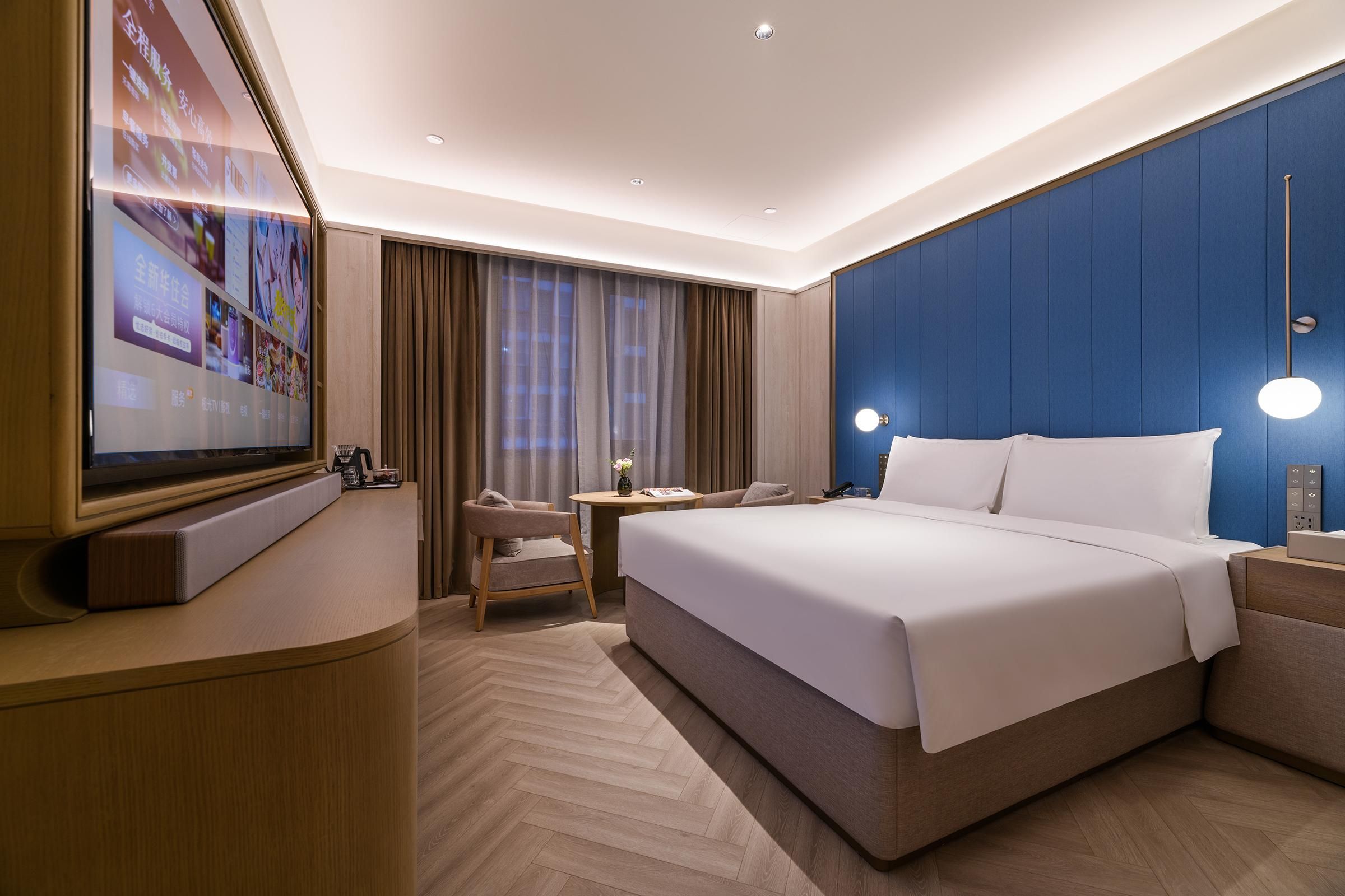 Quarto de hotel moderno com uma cama grande, uma mesa com cadeira, televisão e uma parede azul.