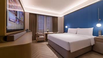 Quarto de hotel moderno com uma cama grande, uma mesa com cadeira, televisão e uma parede azul.
