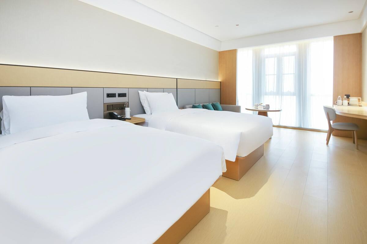 Quarto de hotel com duas camas, uma escrivaninha e uma cadeira.