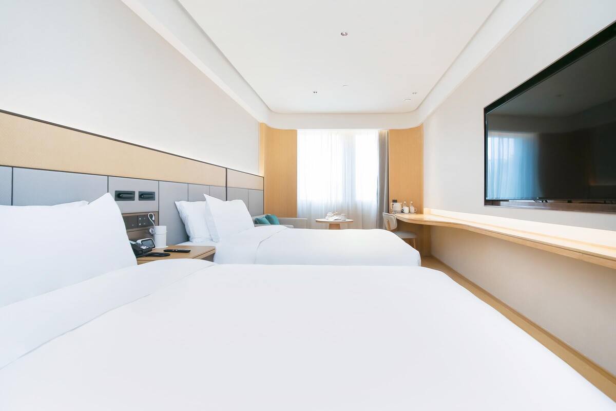 Quarto de hotel com duas camas, uma televisão, uma mesa e uma janela.