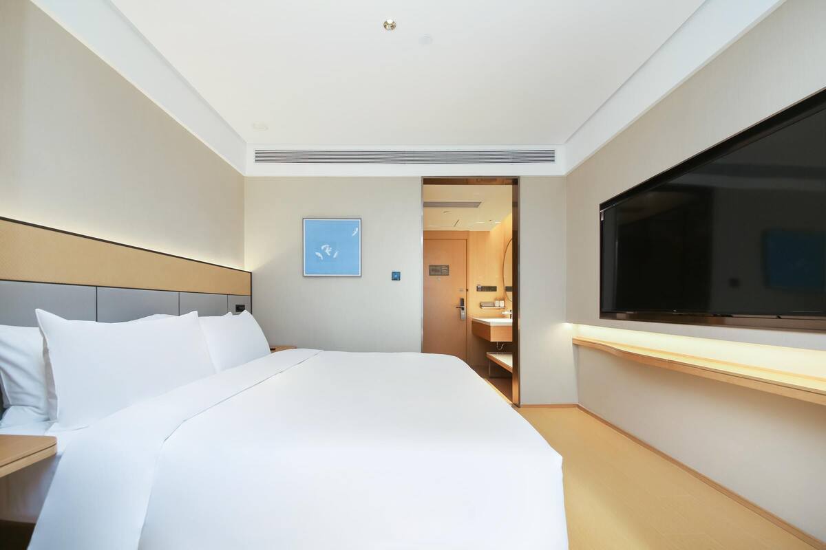 Quarto de hotel com cama, televisão, banheiro e porta que dá para outro cômodo.