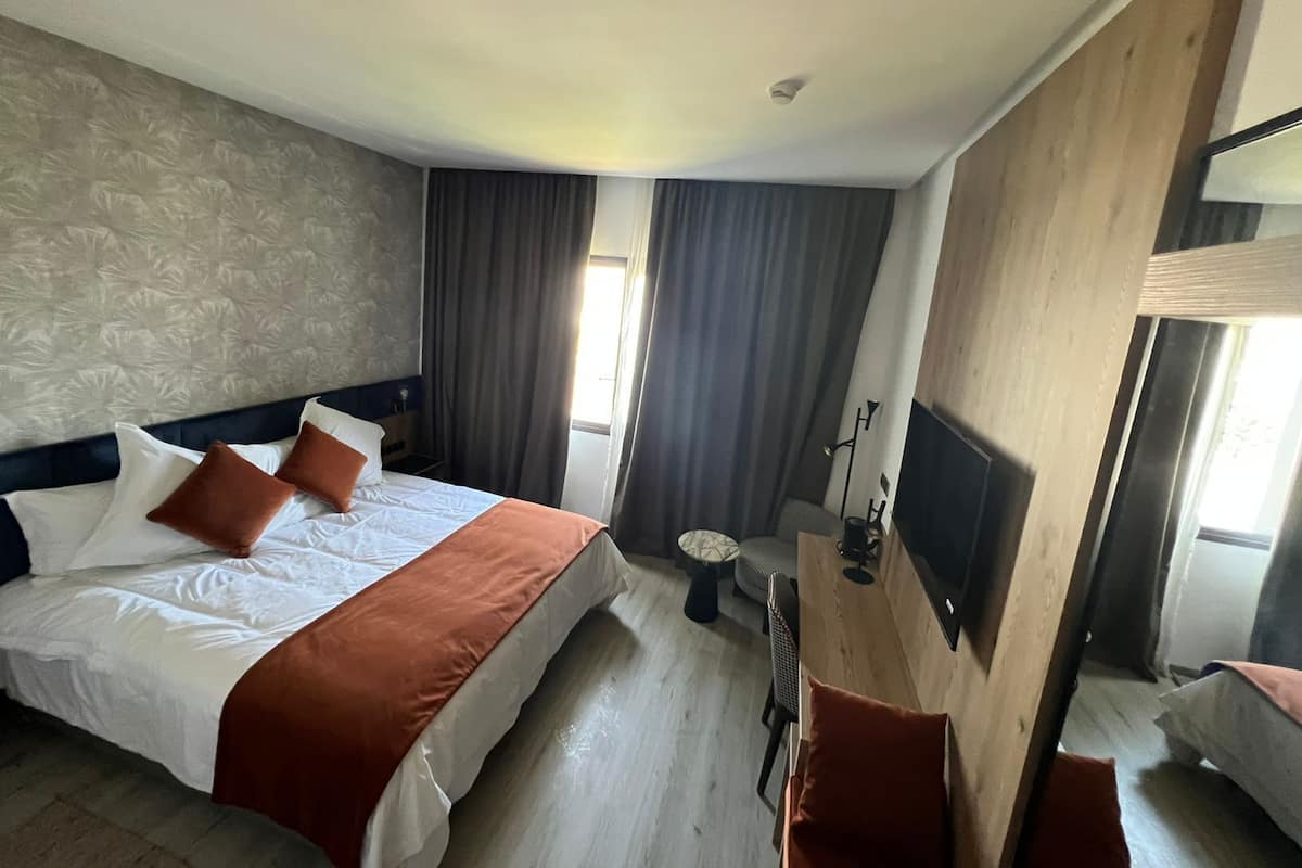 Quarto de hotel com uma cama, televisão, mesa pequena e uma cadeira.