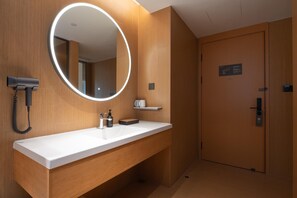 Uma casa de banho moderna com uma sanita branca, um espelho redondo iluminado, um secador de cabelo e uma porta de madeira.