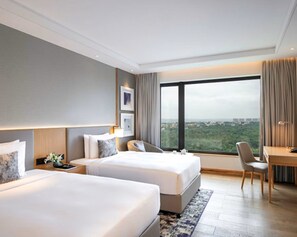 Quarto de hotel com duas camas, uma escrivaninha e uma janela grande com vista para a cidade.