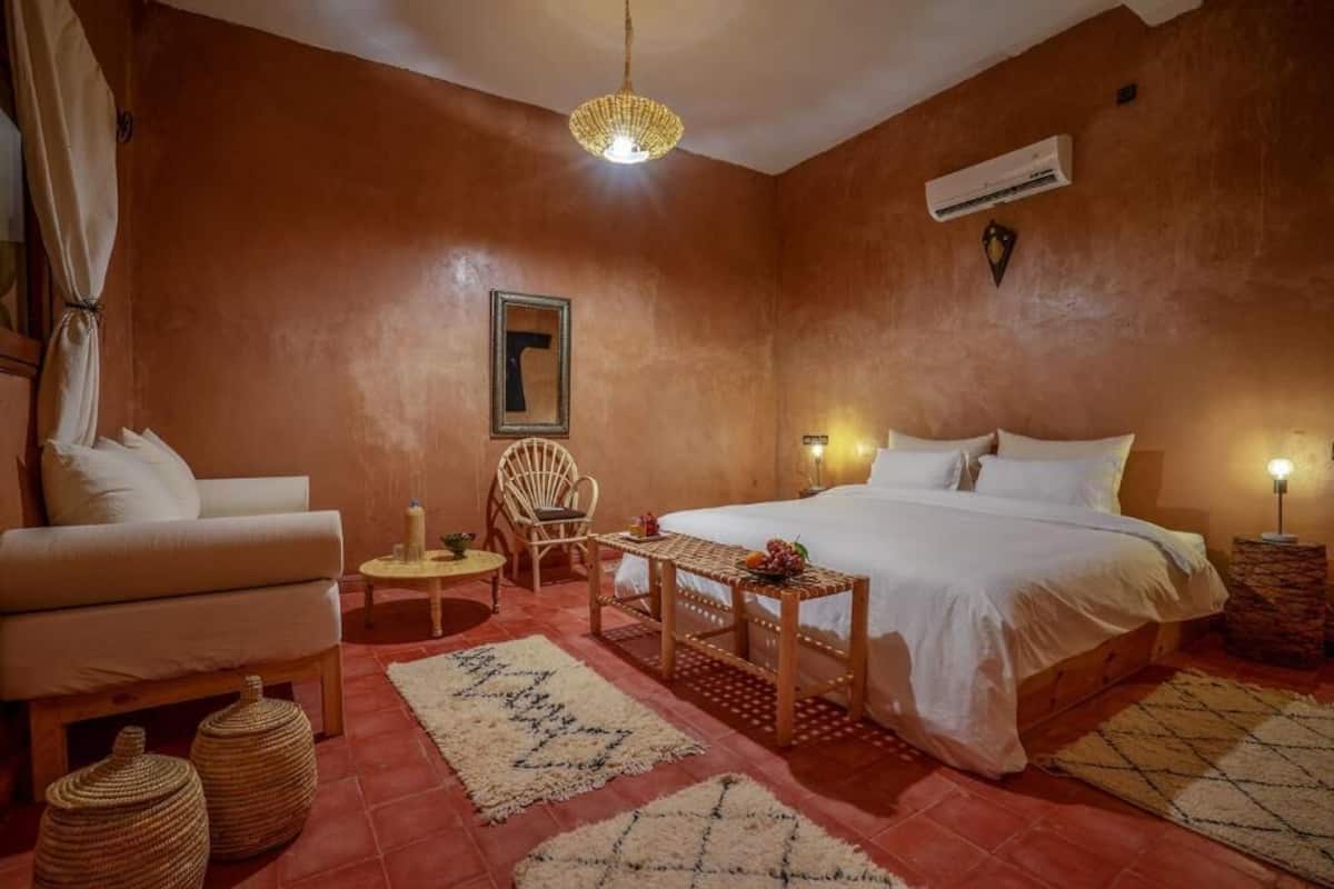 Quarto com cama, uma cadeira, uma mesinha e um lustre.