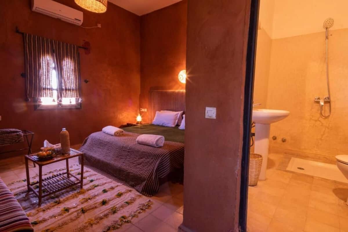 Quarto com cama, mesa de cabeceira e janela com cortinas.
