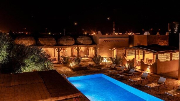 Vista noturna de uma área de piscina com espreguiçadeiras, um edifício com telhado de palha e céu claro.