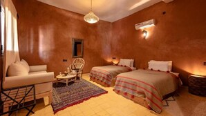 Quarto com duas camas, um sofá, uma mesa pequena, uma cadeira, luminária pendente e aparelho de ar condicionado.