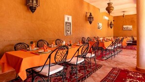 Uma sala de jantar com mesas compridas, cadeiras e lanternas fixadas na parede.