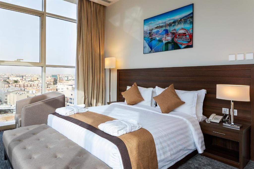 Quarto de hotel com uma cama grande, um sofá, uma escrivaninha e uma janela com vista para a cidade.