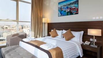 Quarto de hotel com uma cama grande, um sofá, uma escrivaninha e uma janela com vista para a cidade.