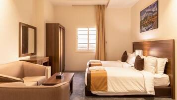 Quarto de hotel com duas camas, um sofá, uma escrivaninha, um espelho, uma janela com cortinas e um quadro na parede.